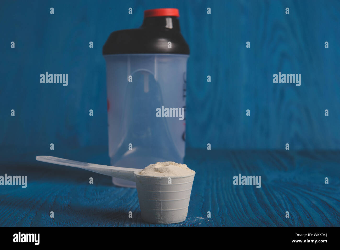 protein supplement powder in plastic spoon on blue wooden background ...