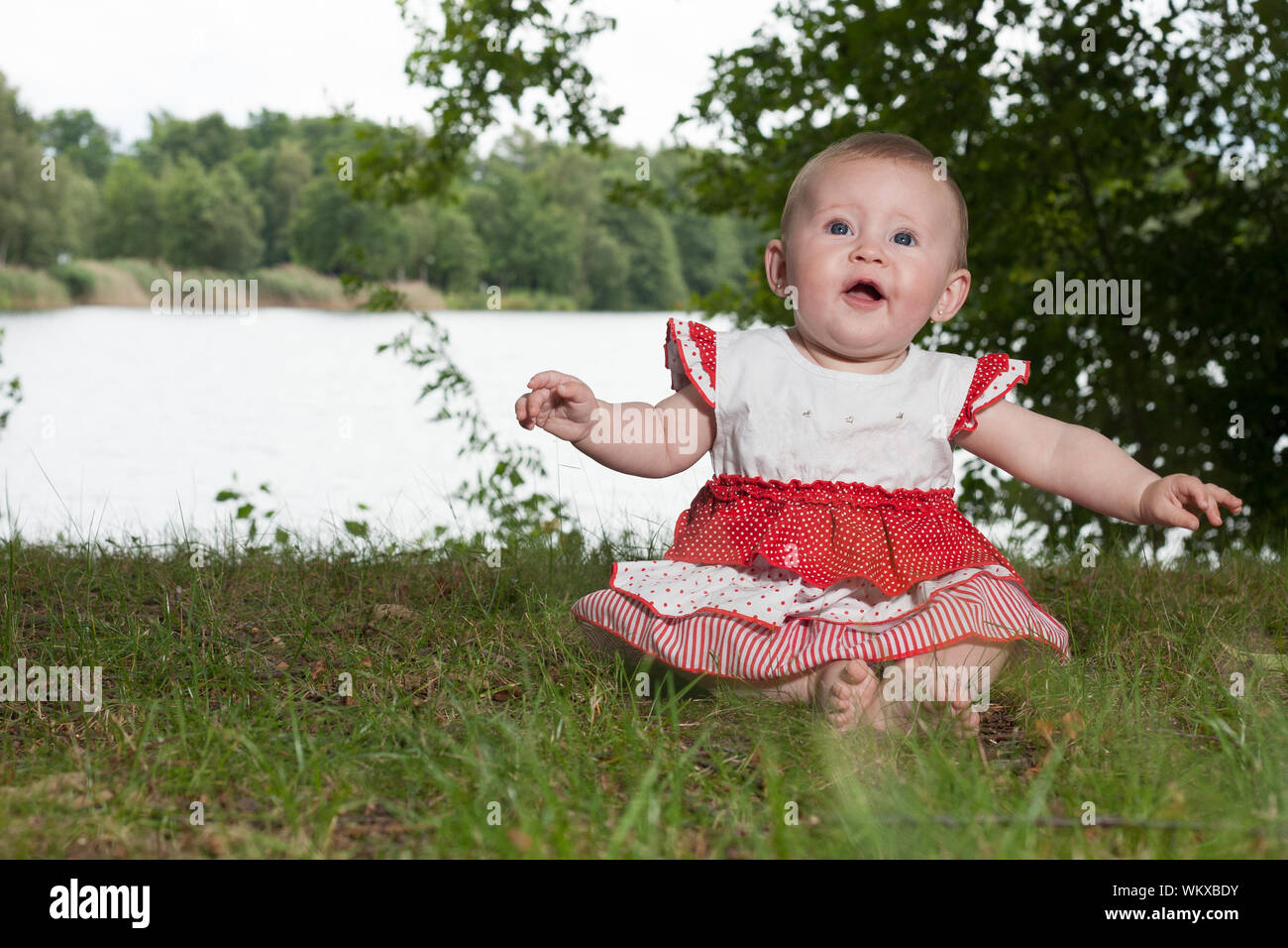 Little baby girl is sitting and playing near the lake Stock Photo - Alamy