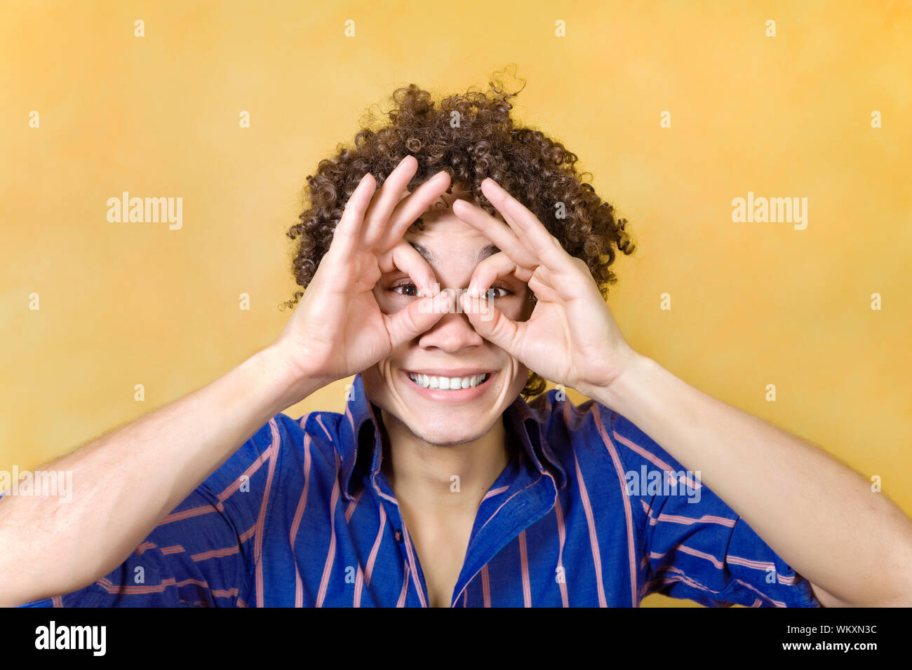 young man with hand over eyes, looking through fingers Stock Photo - Alamy
