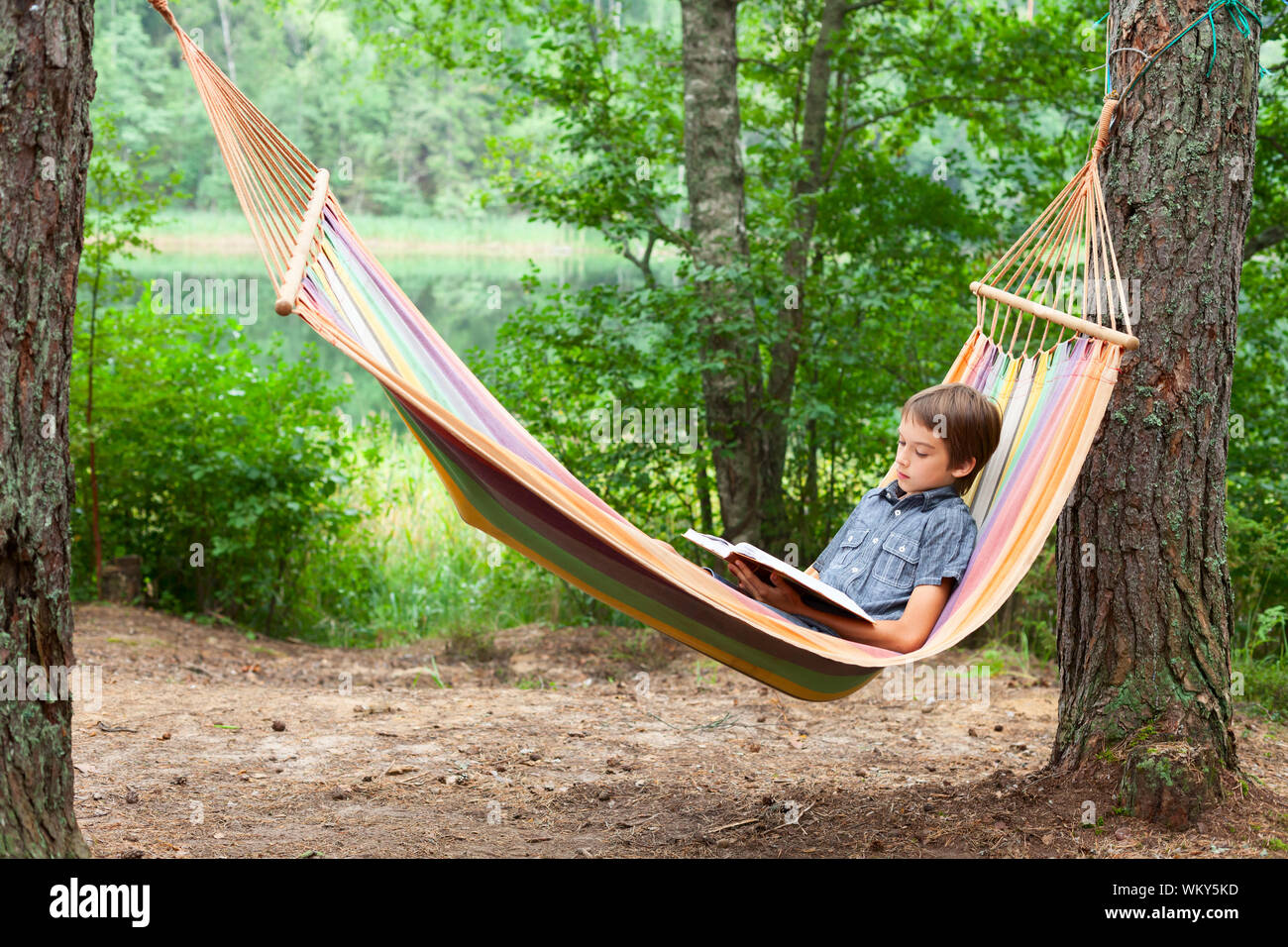 Boy lying in hammock reading a book outdoors Stock Photo - Alamy