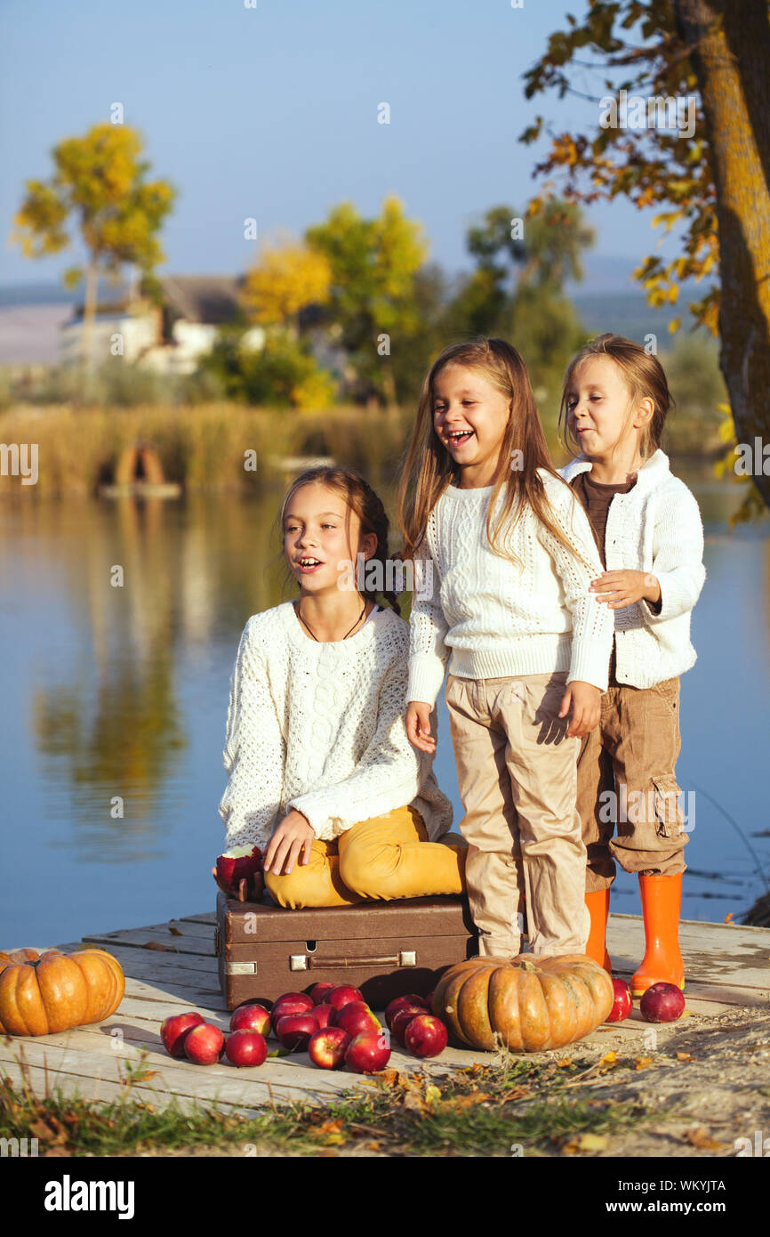 Three cheerful little girls playing on the lake in warm autumn day ...
