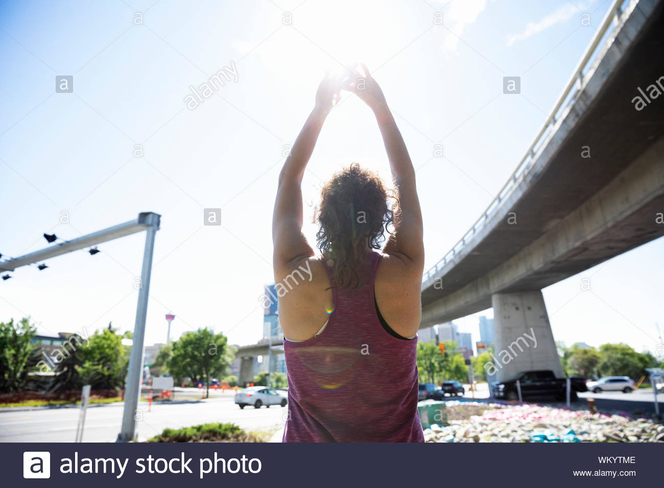 Female runner stretching arms overhead near sunny, urban overpass Stock ...