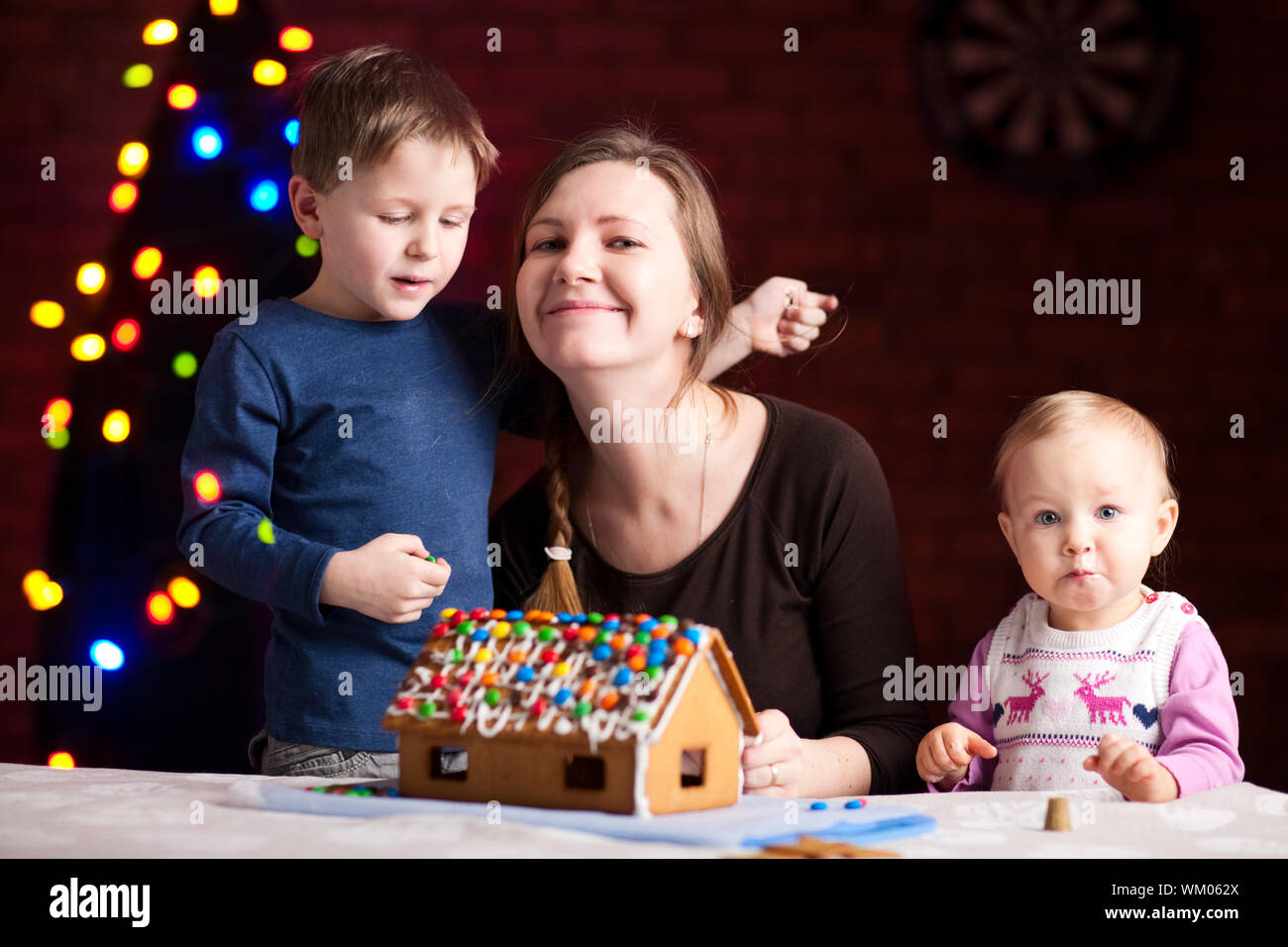 Family decorating gingerbread house on Christmas eve Stock Photo - Alamy
