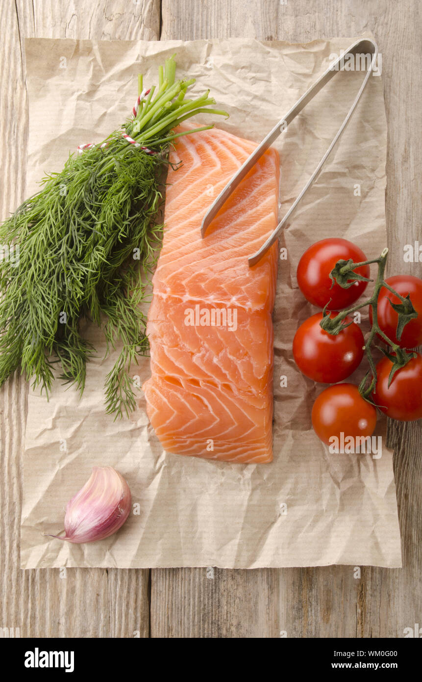 raw salmon fillet with dill, garlic, tomato and fishbone tong on brown ...
