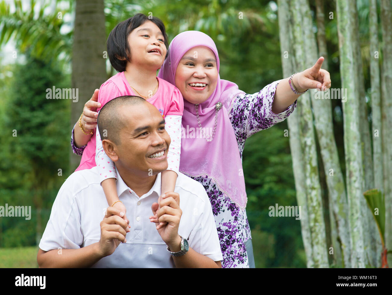 Happy Southeast Asian Muslim family pointing away, outdoor lifestyle at ...