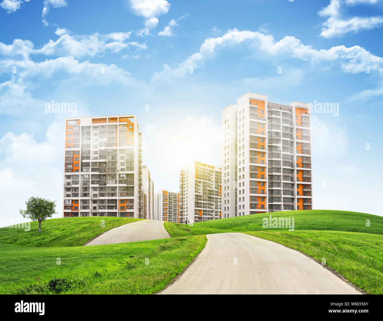Tall buildings, green hills and road against sky with clouds ...
