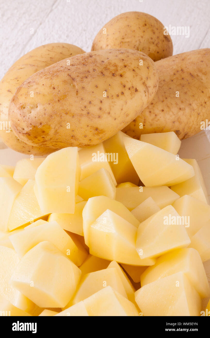 Three Whole Potatoes and Chopped Peeled Pieces on Cutting Board Stock ...