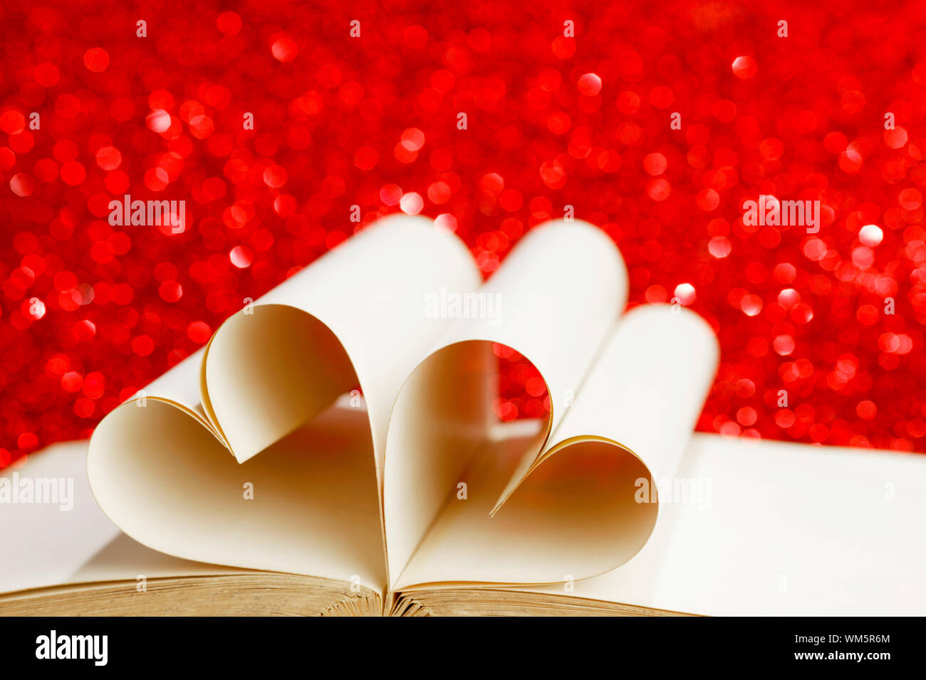 Pages of open book rolled in heart shape on glitter background Stock ...