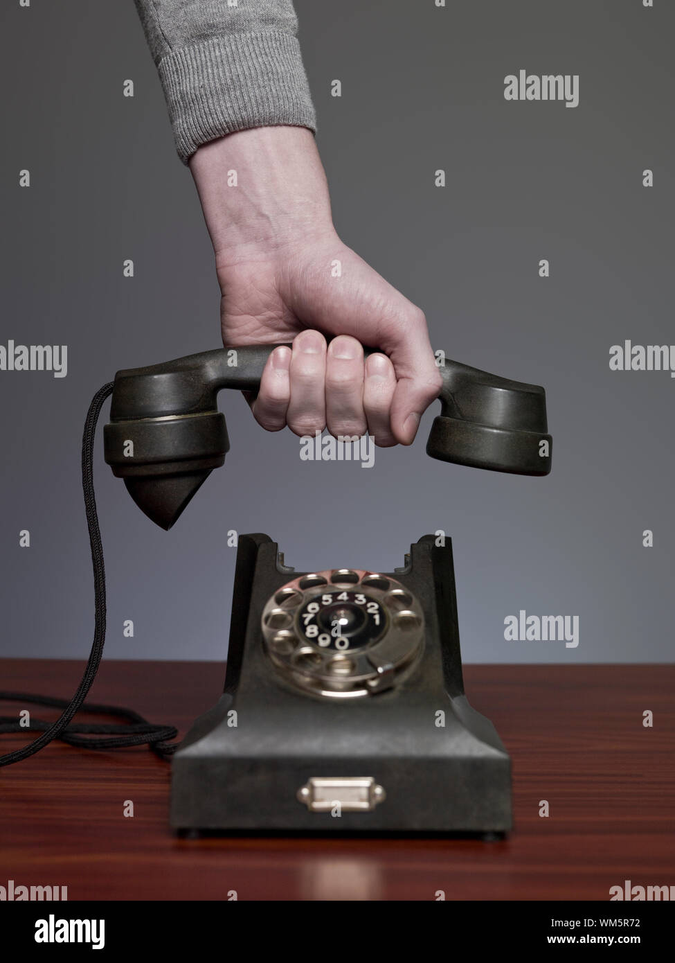Hand picking up retro phone against a grey background Stock Photo - Alamy