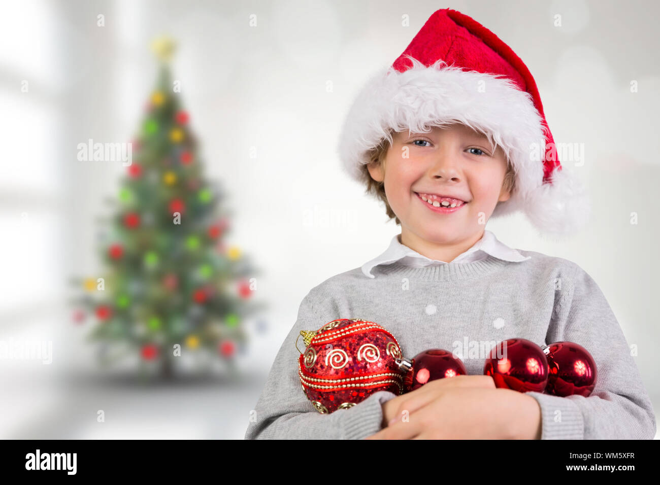 Festive boy smiling against blurry christmas tree in room Stock Photo ...
