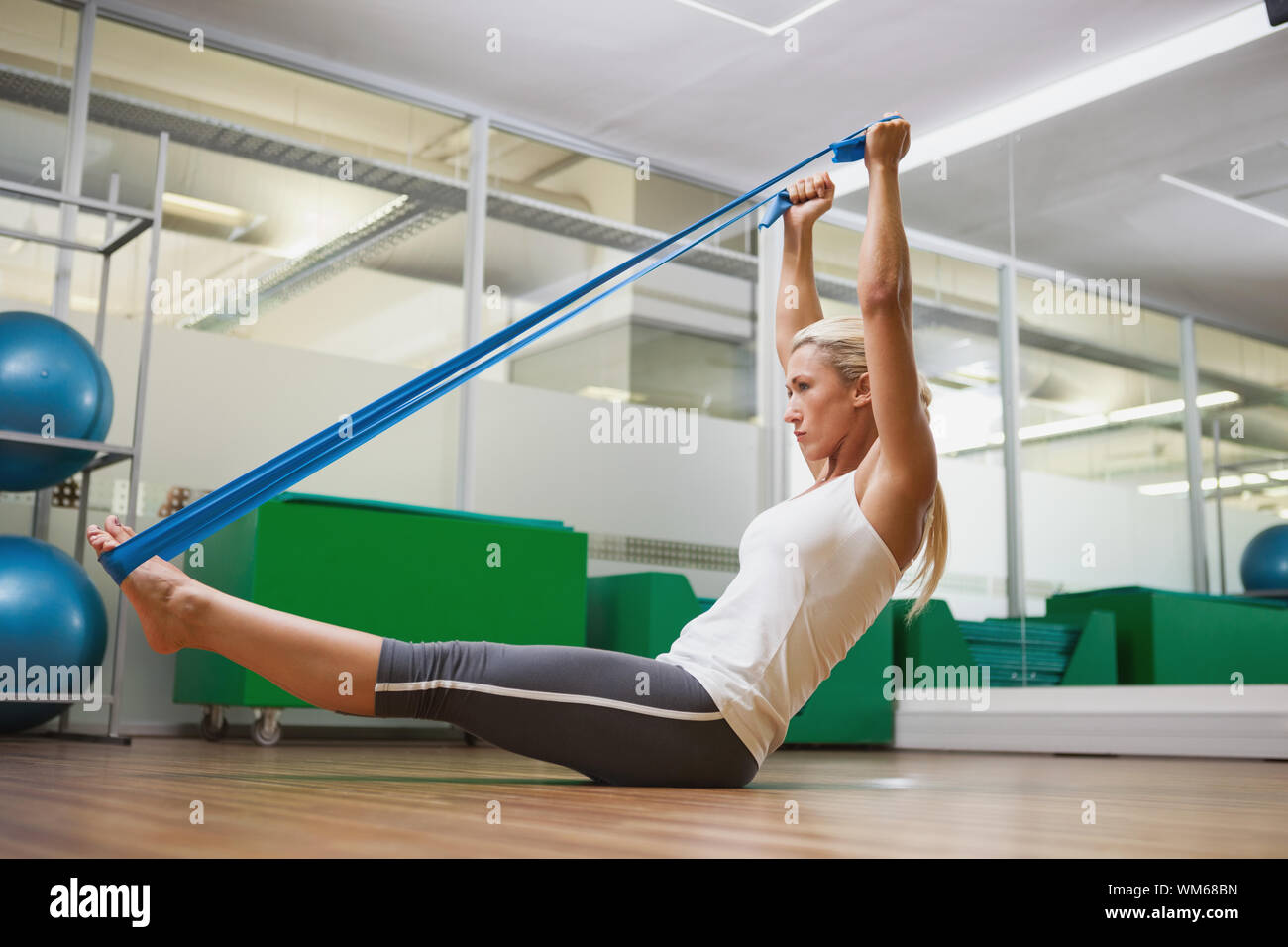 Full length side view of a young woman using resistance band in fitness ...