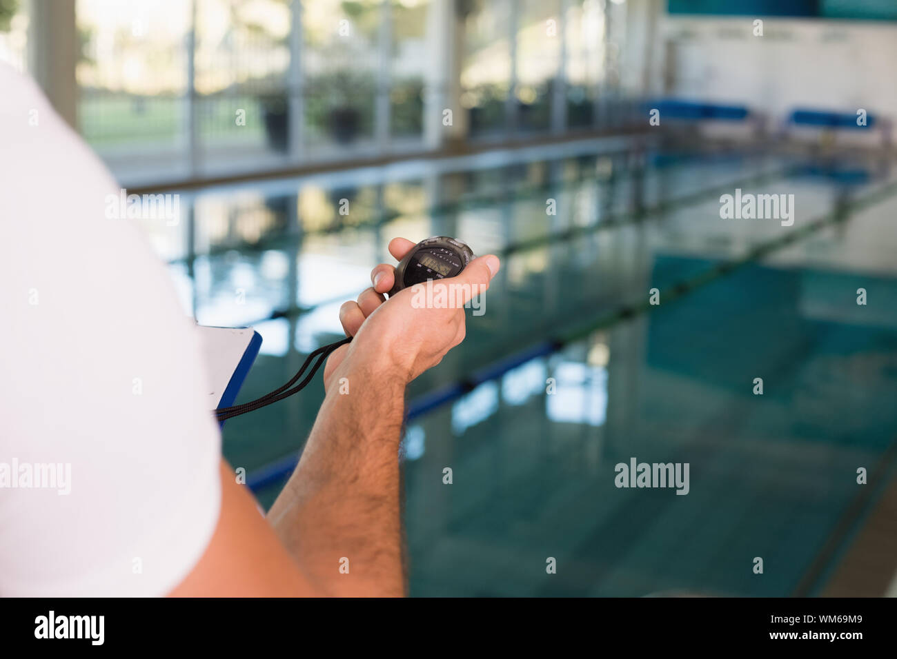 Close up of a cropped swimming coach with stopwatch by the pool at ...