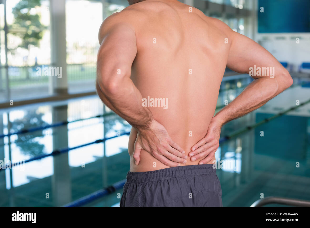 Close up mid section of a shirtless fit swimmer with back ache by the ...