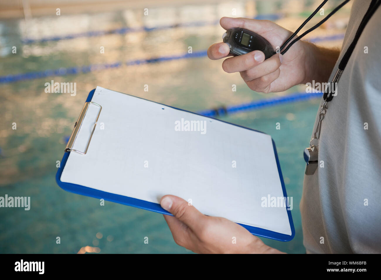 Swimming coach looking at his stopwatch by the pool at the leisure ...