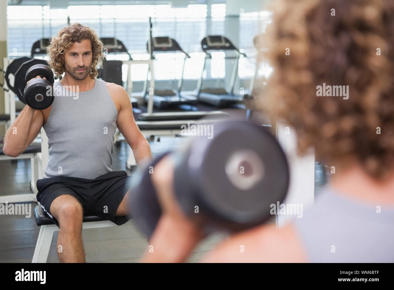 Reflection of a young muscular man exercising with dumbbell in the gym ...