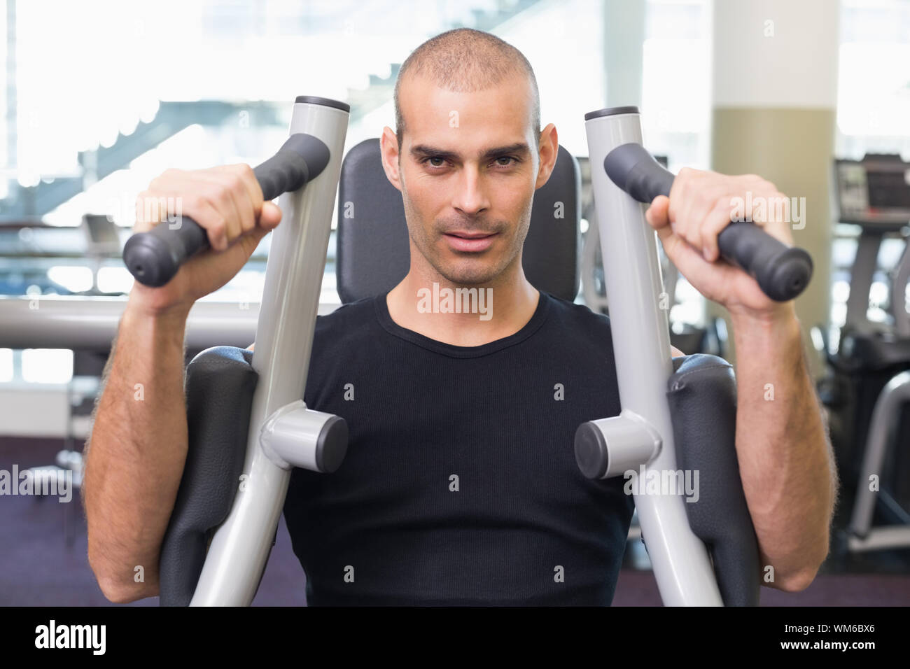 Portrait of a serious young man working on fitness machine at the gym ...