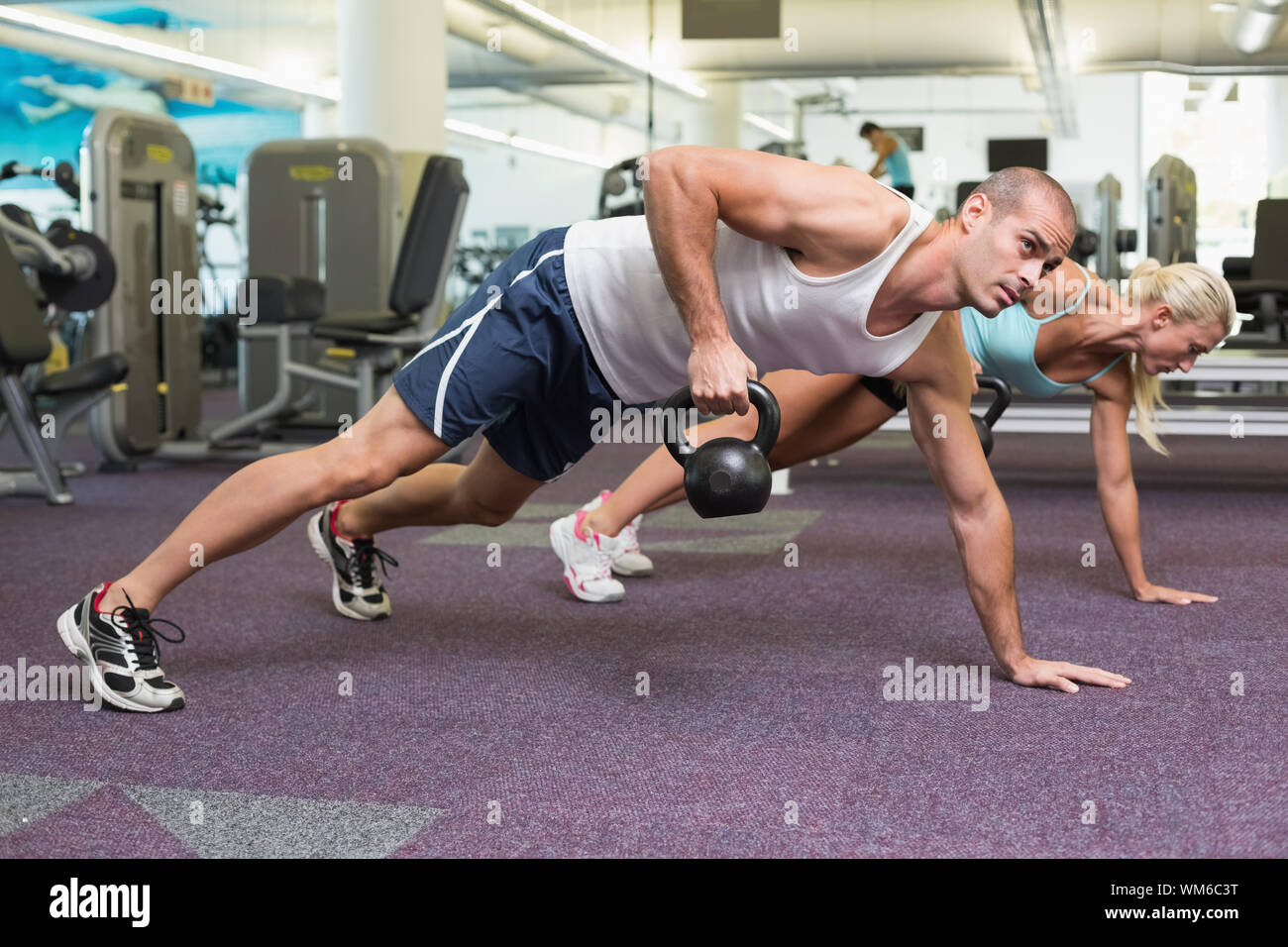 Side view of a fit couple doing push ups with kettle bells in the gym ...