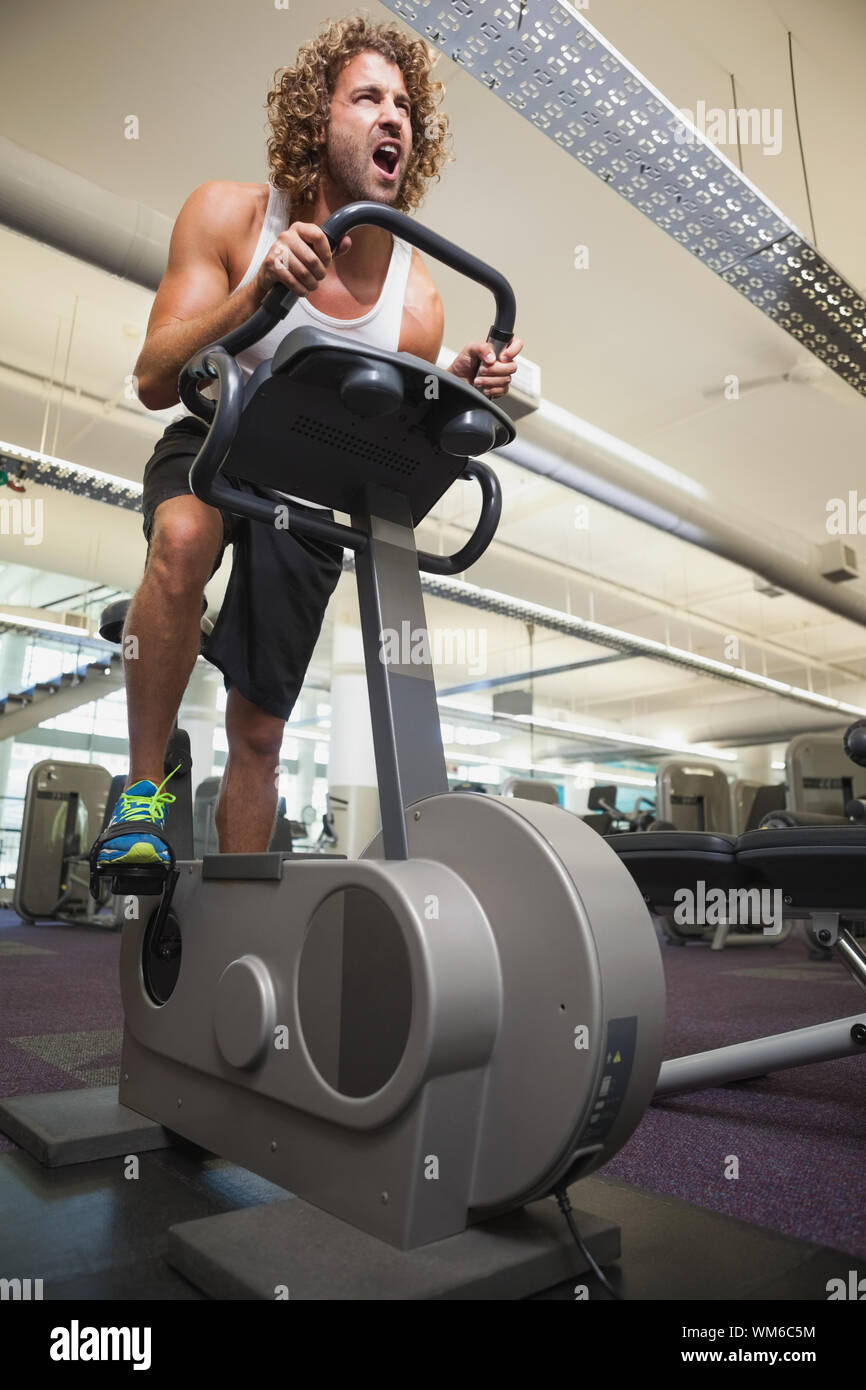 Determined handsome young man working out on exercise bike at the gym ...