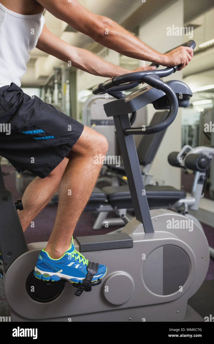 Side view of a cropped man working out on exercise bike at the gym ...