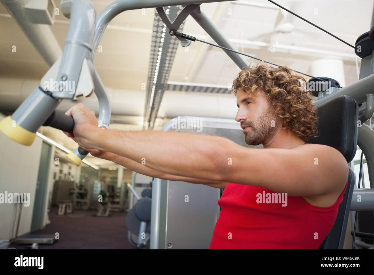 Side view of a handsome young man working on fitness machine at the gym ...