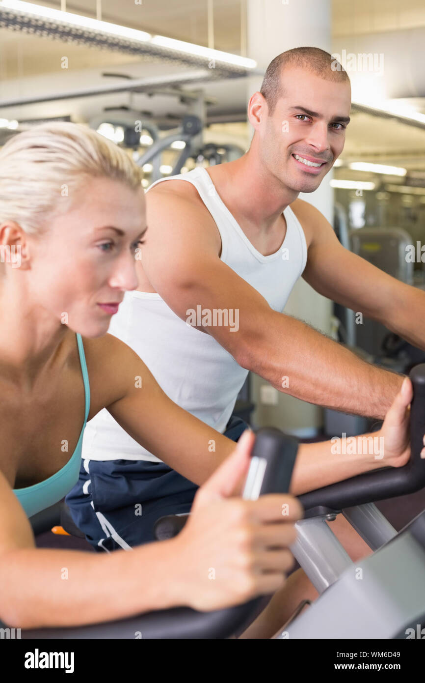 Side view of a fit young couple working on exercise bikes at the gym ...