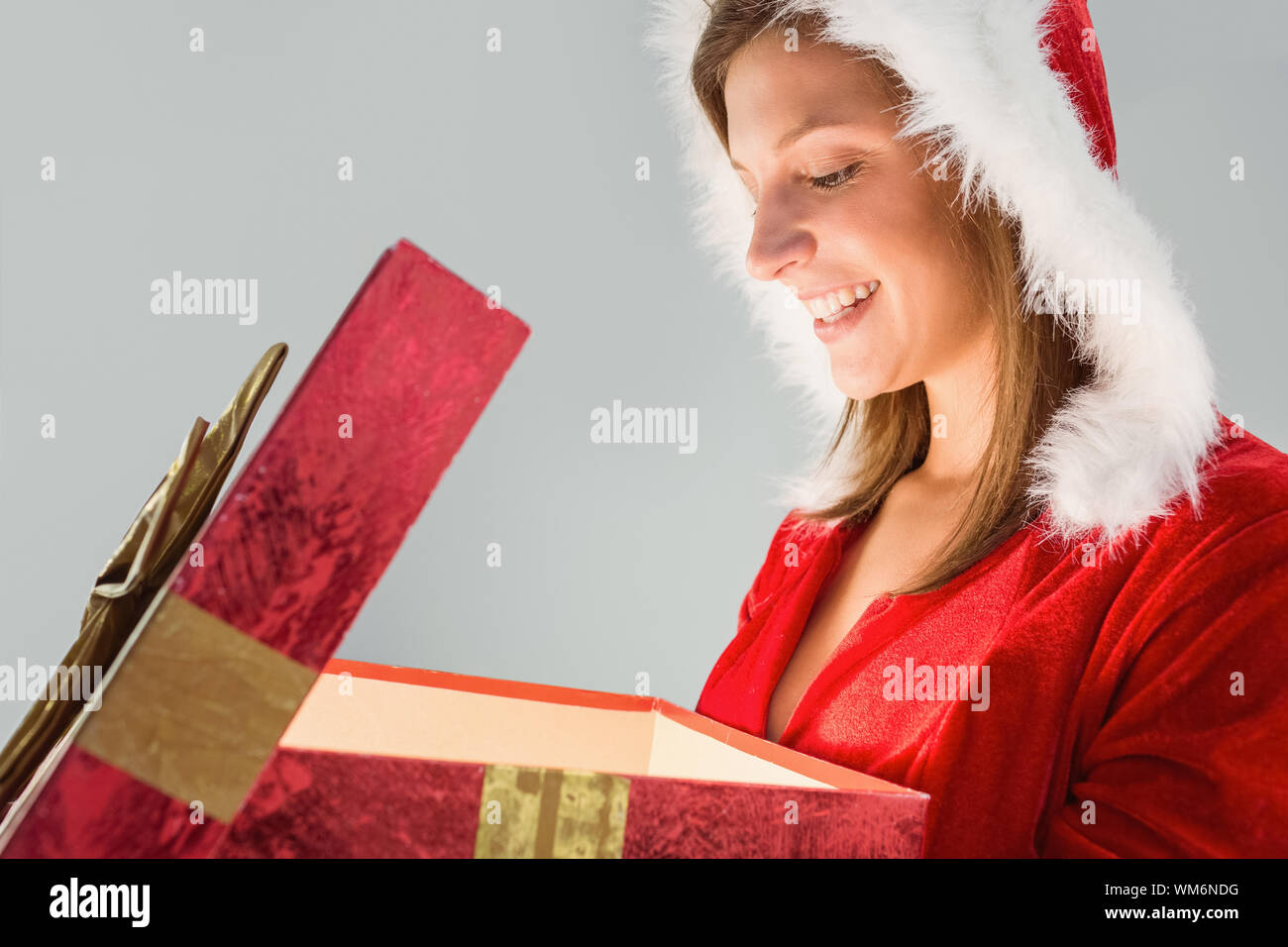 Pretty santa girl opening a gift on gray background Stock Photo - Alamy