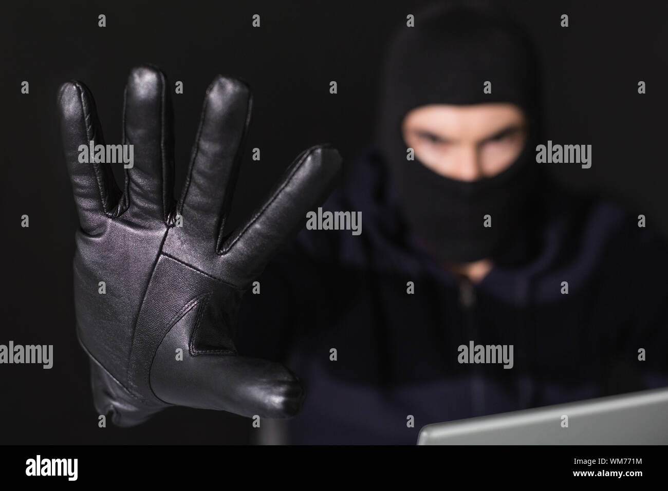 Hacker in balaclava with fingers spread out on black background Stock ...
