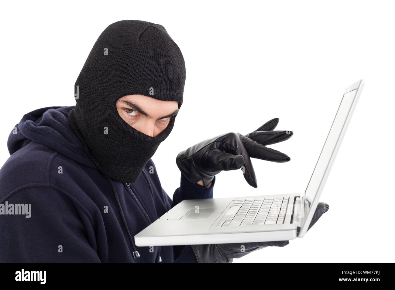 Hacker in balaclava standing and typing on laptop on white background ...