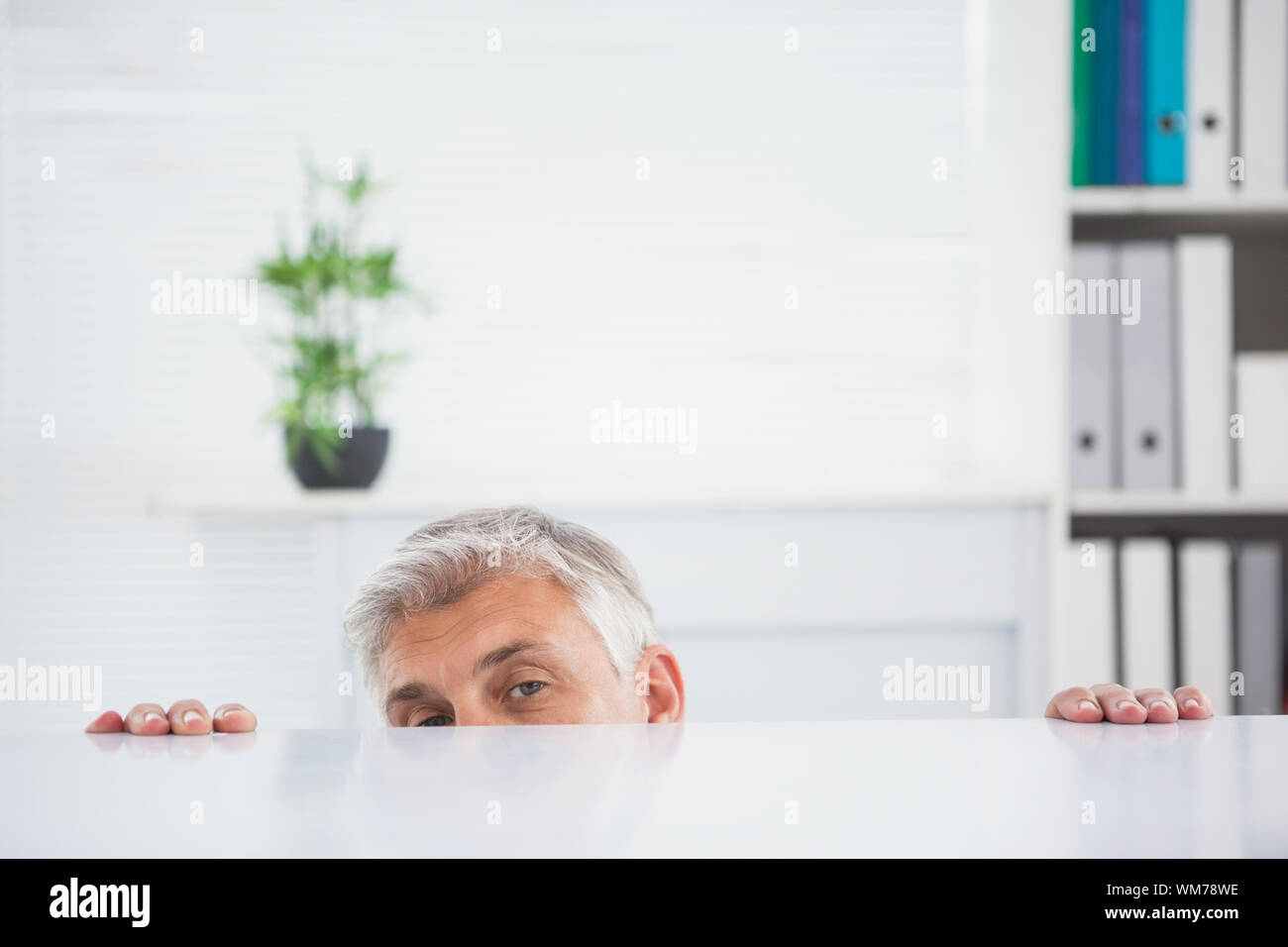 Nervous businessman peeking over desk in his office Stock Photo - Alamy