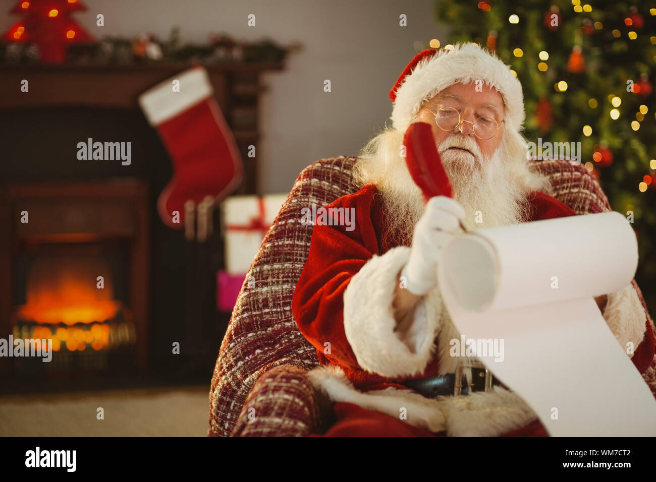 Concentrated santa writing his list on a scroll at home in the living ...