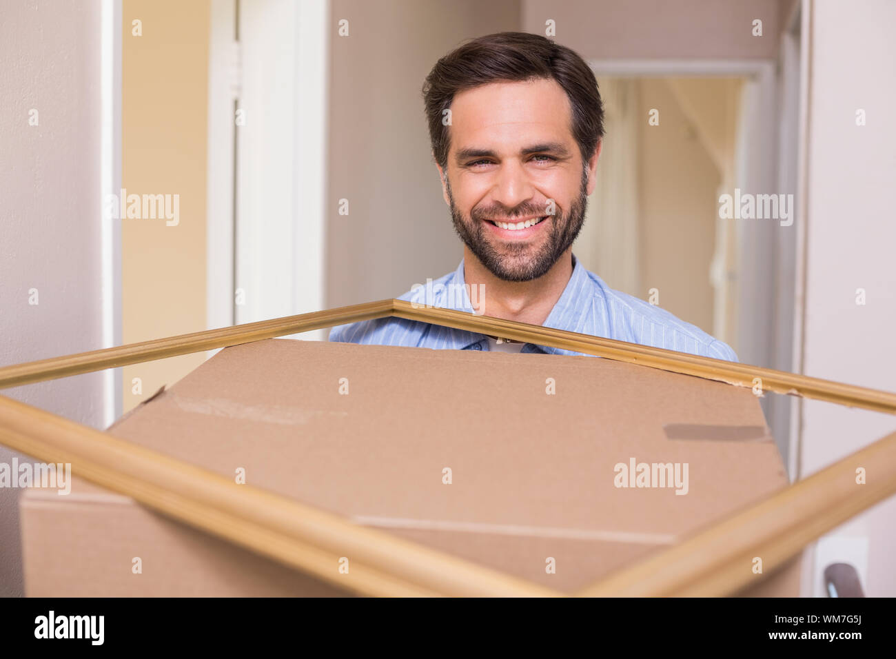Happy man carrying moving box and frame in his new home Stock Photo - Alamy