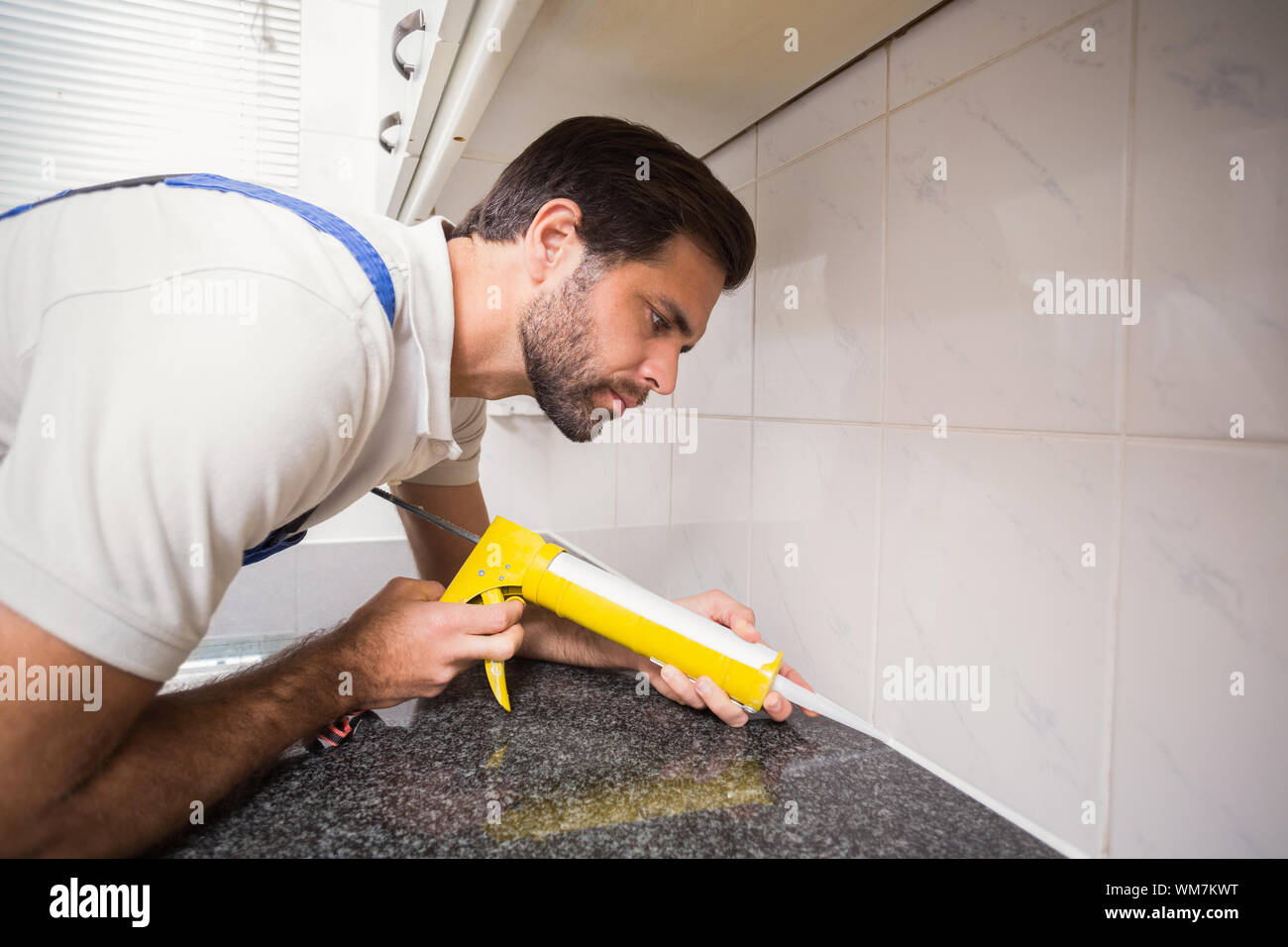 Plumber putting filling in between tiles in the kitchen Stock Photo - Alamy