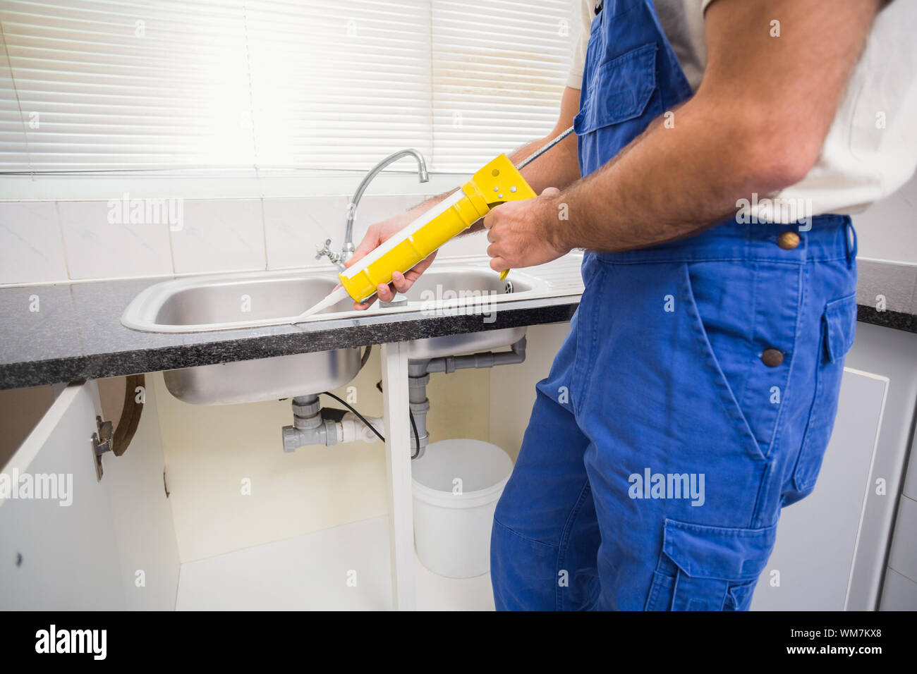 Plumber putting filling in between tiles in the kitchen Stock Photo - Alamy