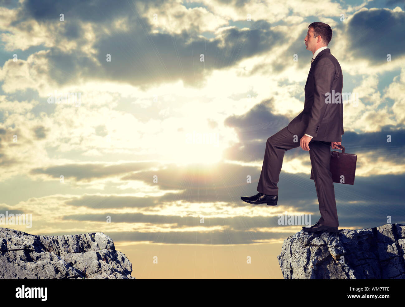 Businessman standing on the edge of rock gap, lifting his foot as if ...