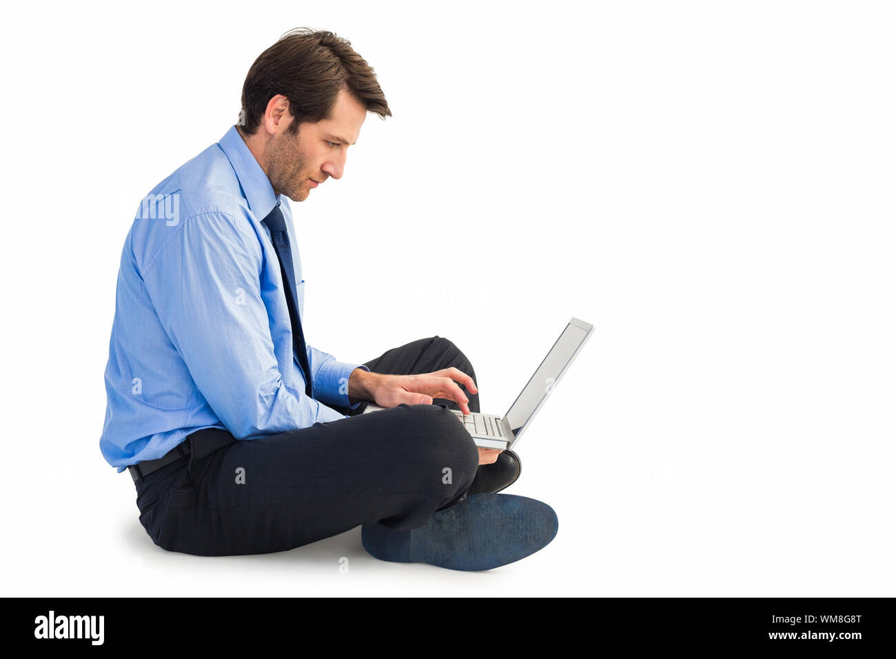 Businessman sitting on floor working on laptop on white background ...