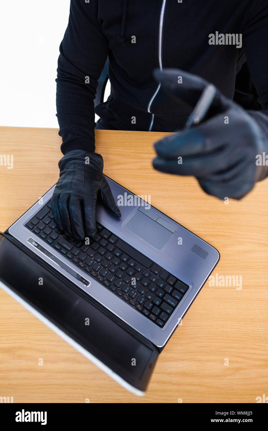 Mid section of a burglar using laptop and smartphone on white ...