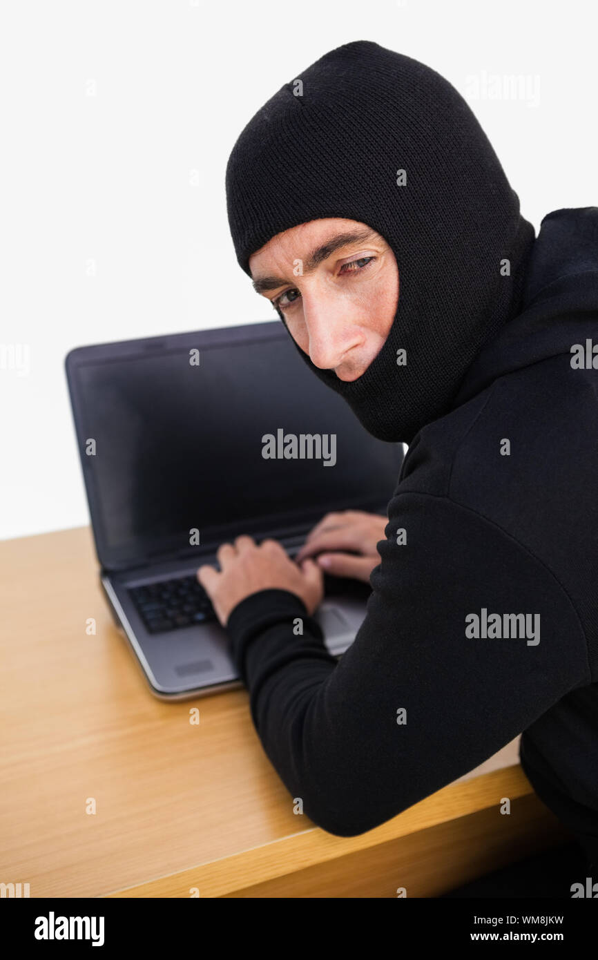 Burglar hacking a laptop and looking behind him on white background ...