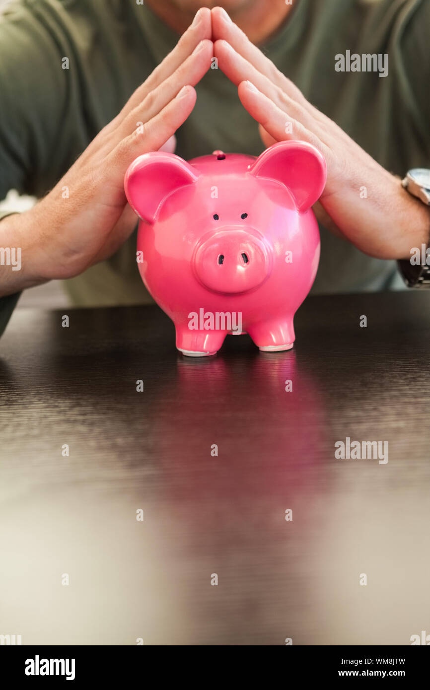 Mid section of a man with joined hands on piggy bank at home in the ...