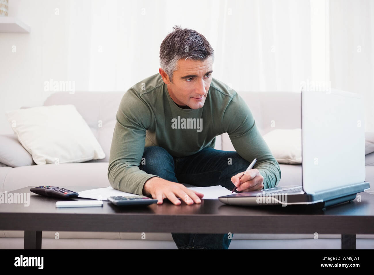 Concentrated man using laptop and taking notes at home in the living ...