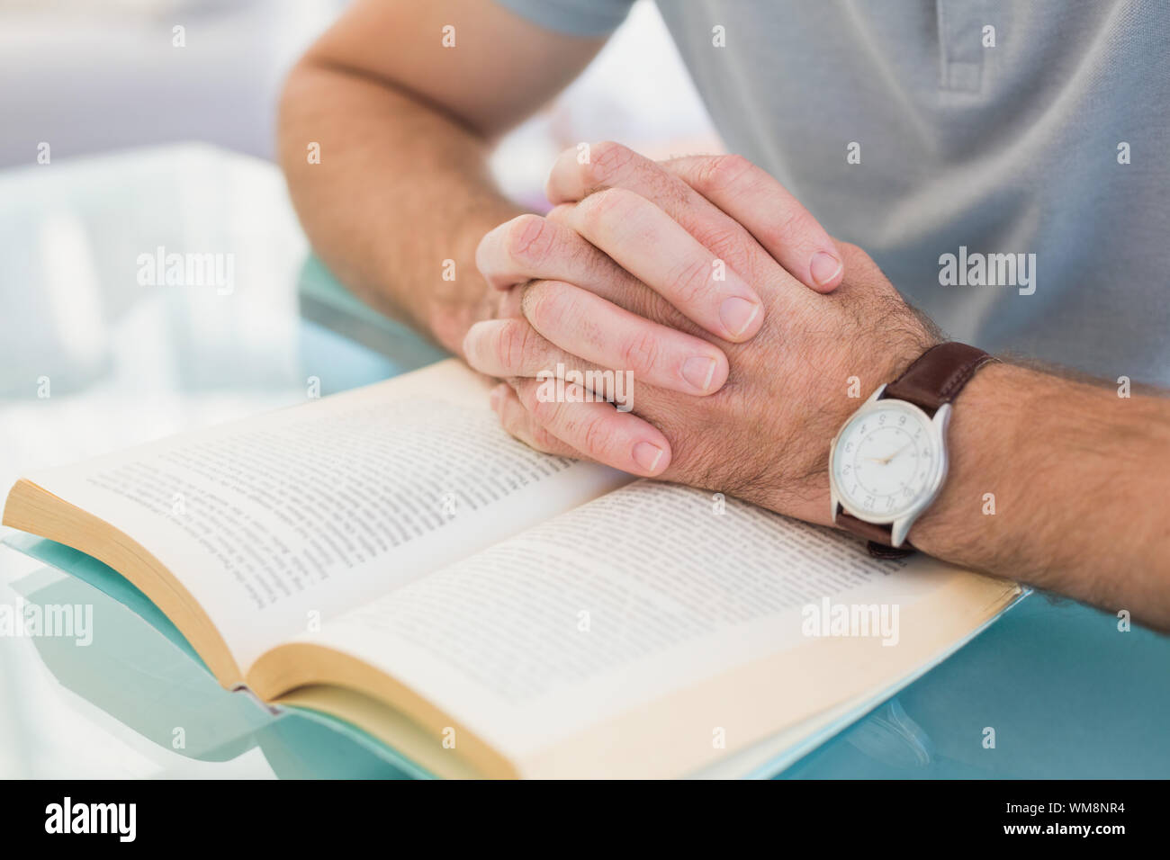 Casual businessman sitting at desk reading a book puting is hands ...