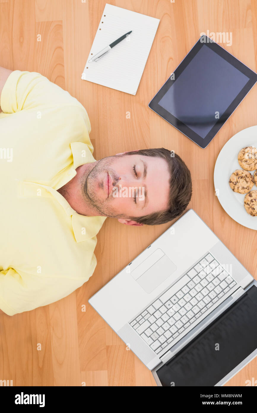 Man lying on floor surrounded by various objects at home in the living ...