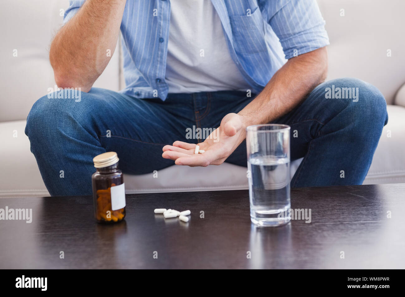 Man taking his pills on couch in the living room Stock Photo - Alamy