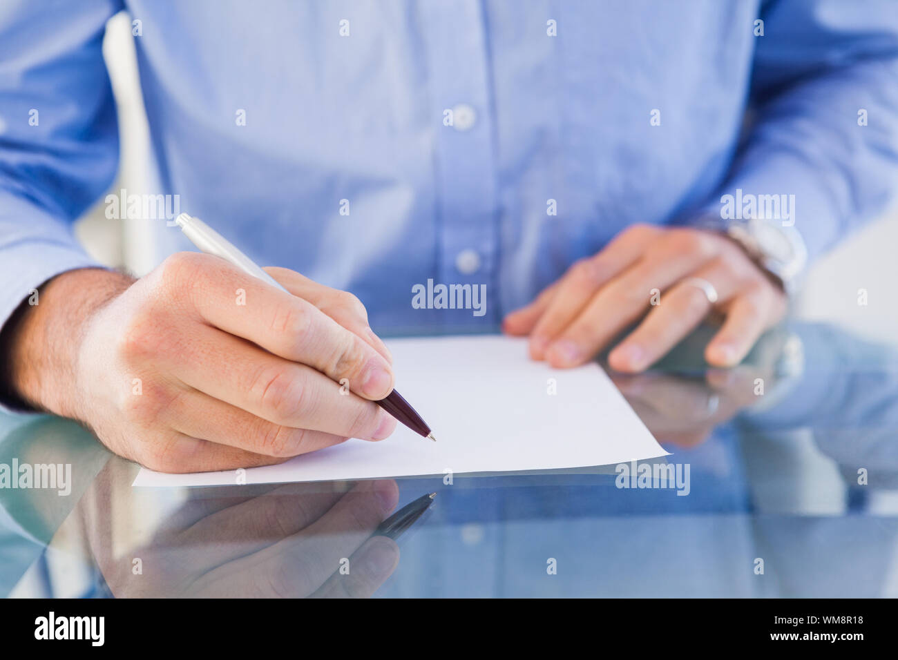 Businessman sitting at desk writing in the office Stock Photo - Alamy