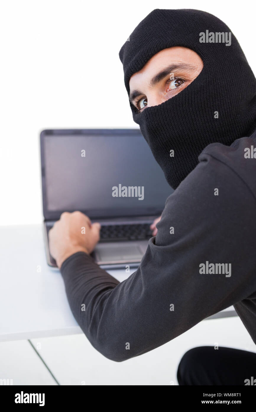 Burglar hacking into laptop while looking at camera on white background ...
