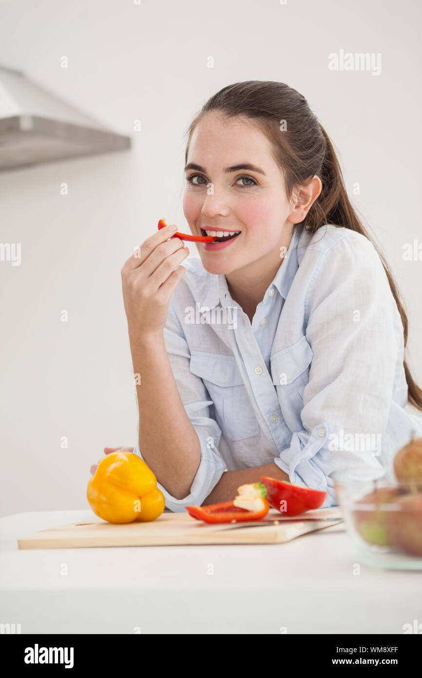 Pretty brunette eating sliced pepper at home in the kitchen Stock Photo ...