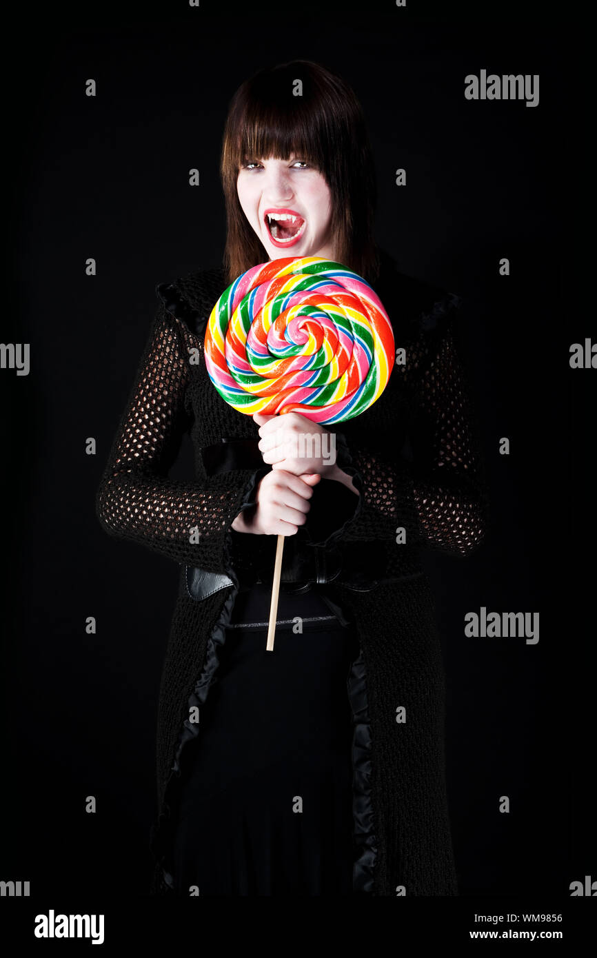 Vampire girl biting into a colorful lollipop Stock Photo - Alamy