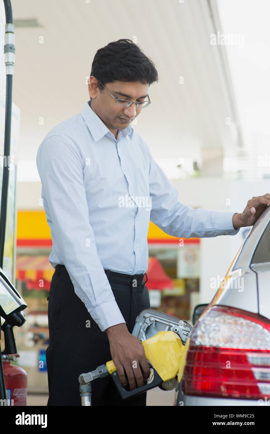 Pumping gas. Asian Indian man pumping gasoline fuel in car at gas ...