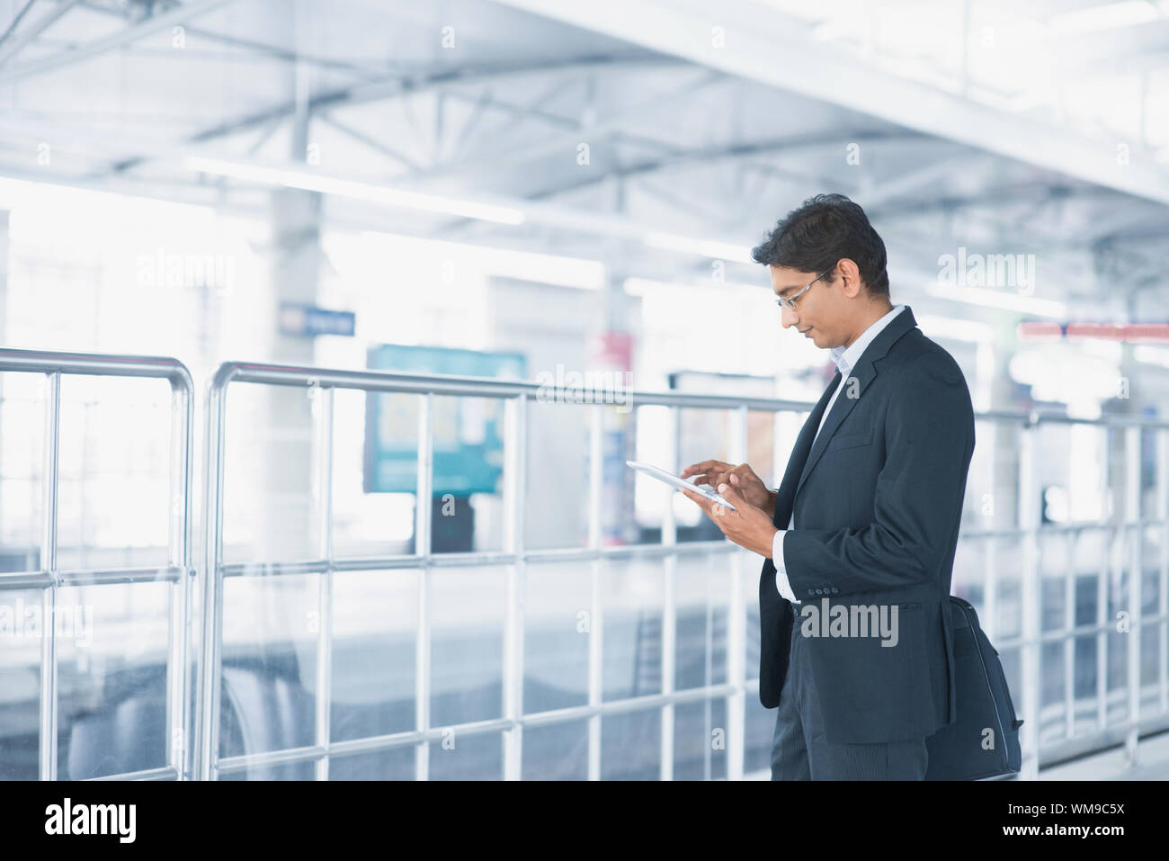 Asian Indian businessman using tablet computer while waiting train at ...