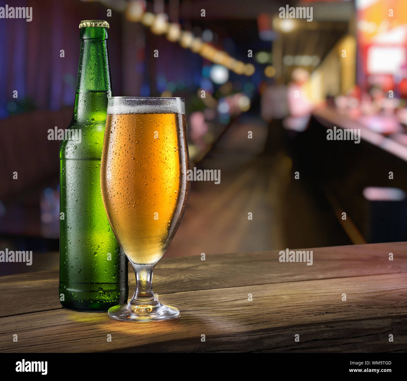 Glass of light beer and green beer bottle on the bar counter. Behind ...