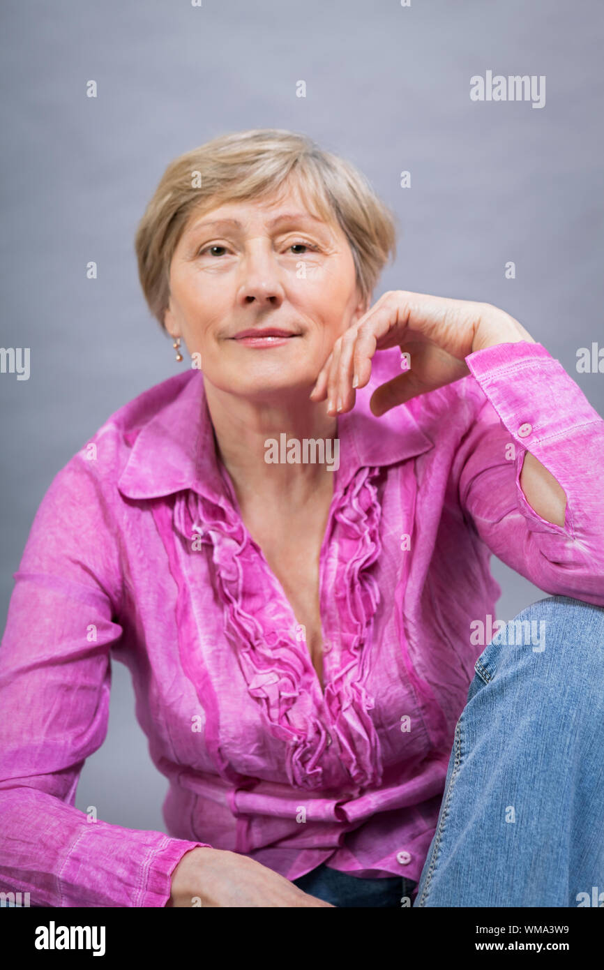 Beautiful blond trendy senior woman posing in a pink blouse and jeans ...